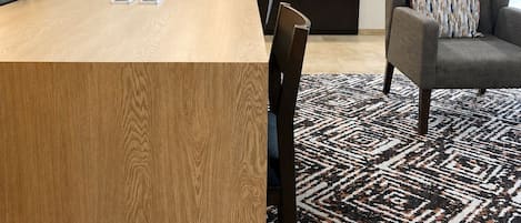Quarto de hotel moderno com área de refeições, tapete estampado e poltrona cinza.