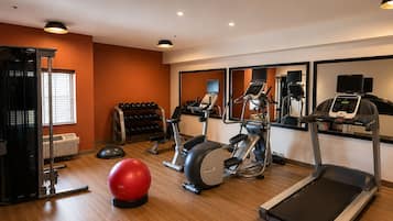 Academia com esteiras, elíptico, bicicleta ergométrica, bola de exercício vermelha e um suporte de halteres.