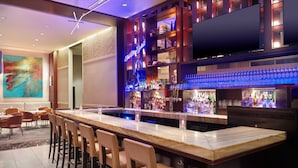 Uma área de bar com um balcão extenso, vários bancos e uma televisão montada acima.