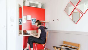 Quarto com uma parede de destaque vermelha, uma escrivaninha com um laptop, uma cadeira e um banco de madeira.