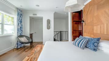 Quarto com cama, cadeira, cabeceira de madeira, luminária pendente e vista para uma escada.