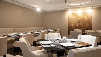 Uma área de refeições moderna com mesas redondas, cadeiras acolchoadas e um painel decorativo.