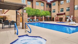 Uma área de piscina de hotel com hidromassagem, espreguiçadeiras e um alpendre coberto.