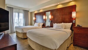 Quarto de hotel com duas camas, televisão, cómoda de madeira e um espelho grande.