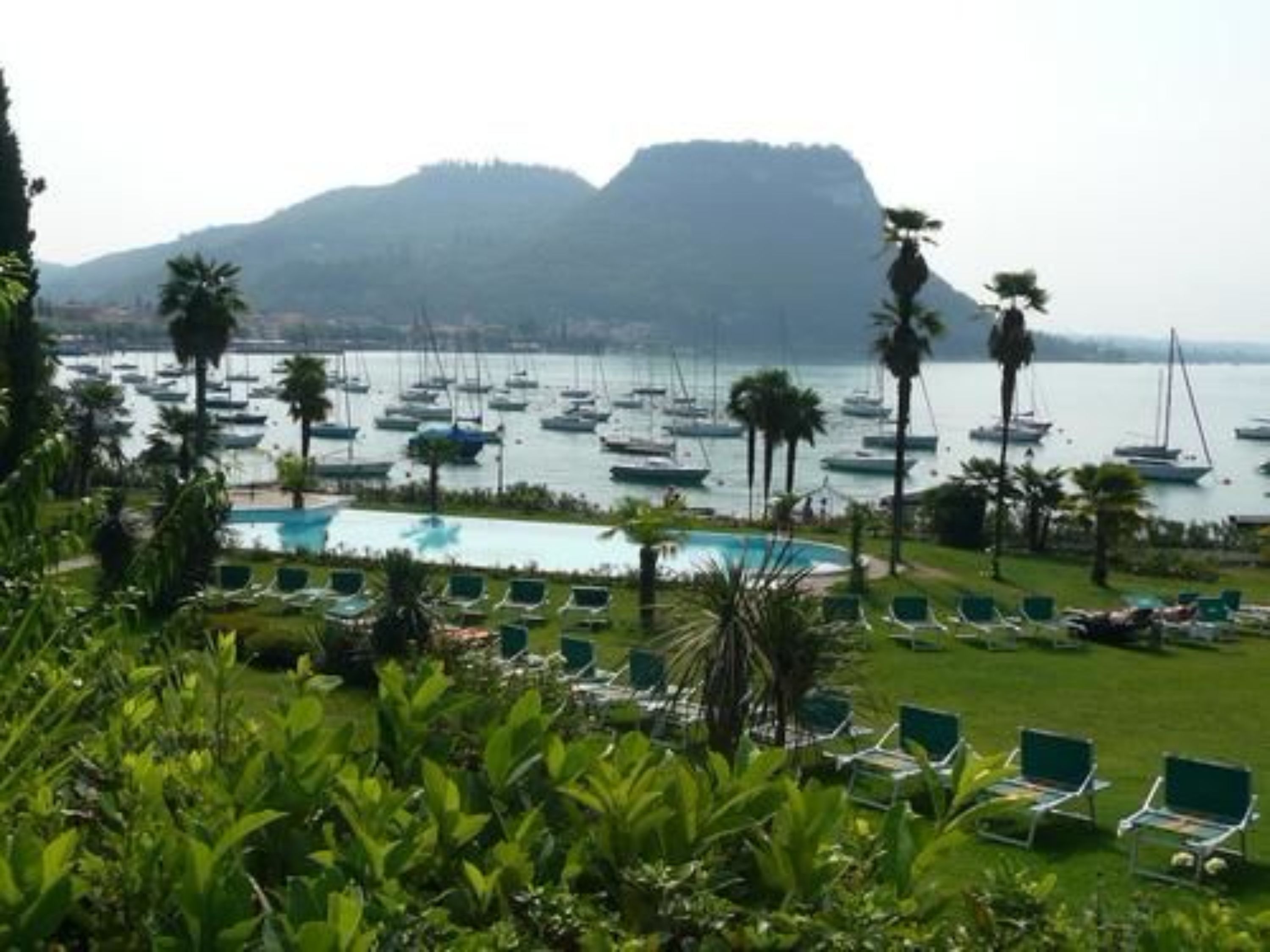 Um resort com piscina, espreguiçadeiras e barcos ao fundo.