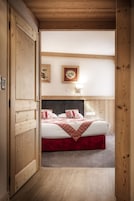 Quarto com teto de madeira, cama com roupa de cama vermelha, cabeceira e luminária fixada na parede.