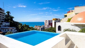 Uma piscina azul límpida com vista para o oceano e edifícios ao fundo.