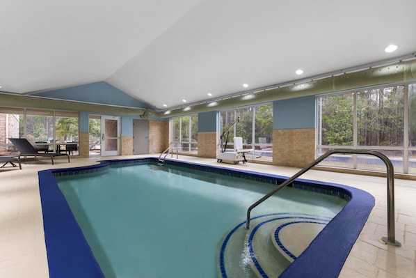 Piscina interna com água azul cristalina, área de estar com cadeiras e janelas amplas com vista para o exterior.