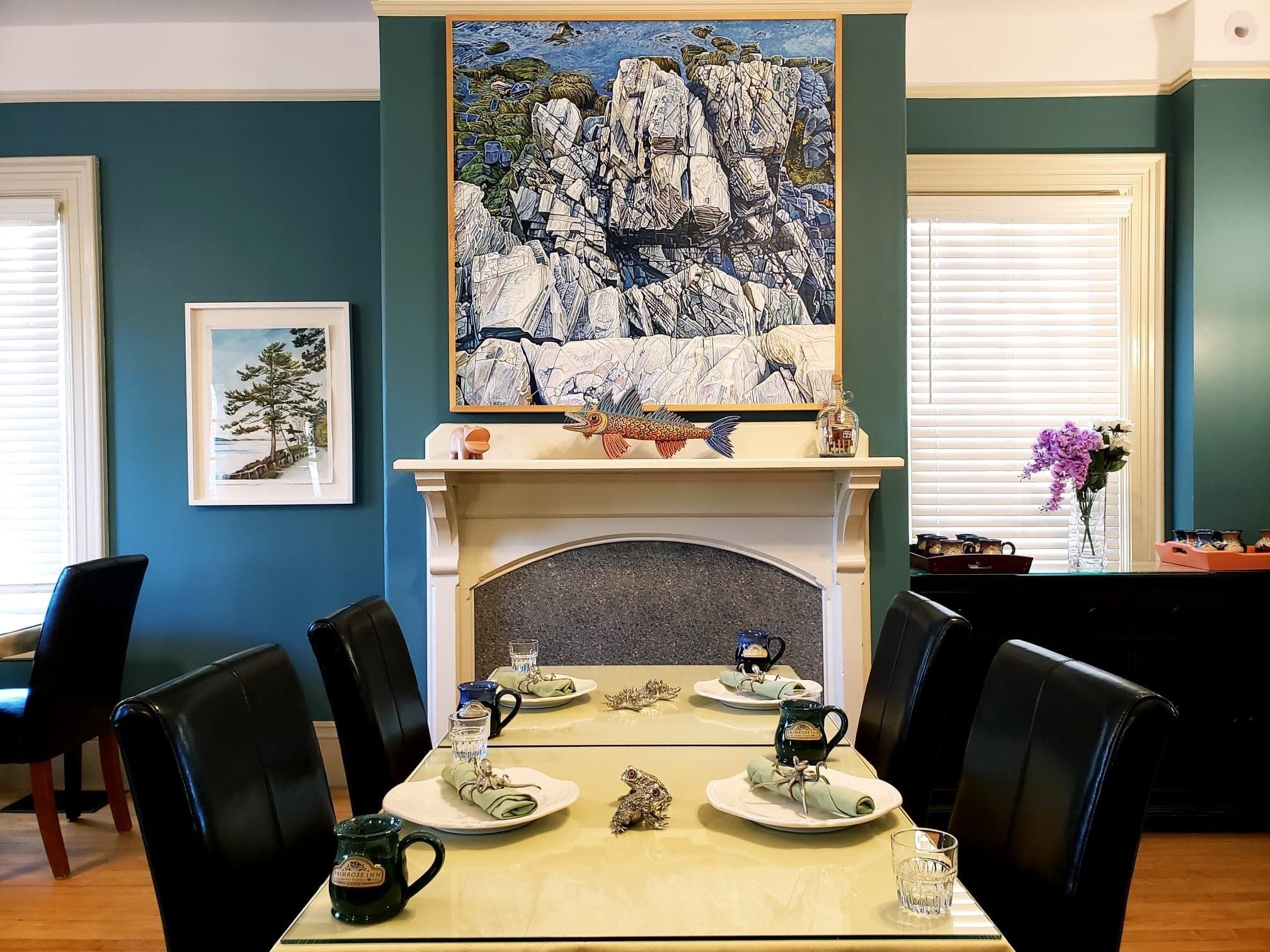 Uma sala de jantar com uma mesa posta para quatro pessoas, lareira e obras de arte nas paredes.
