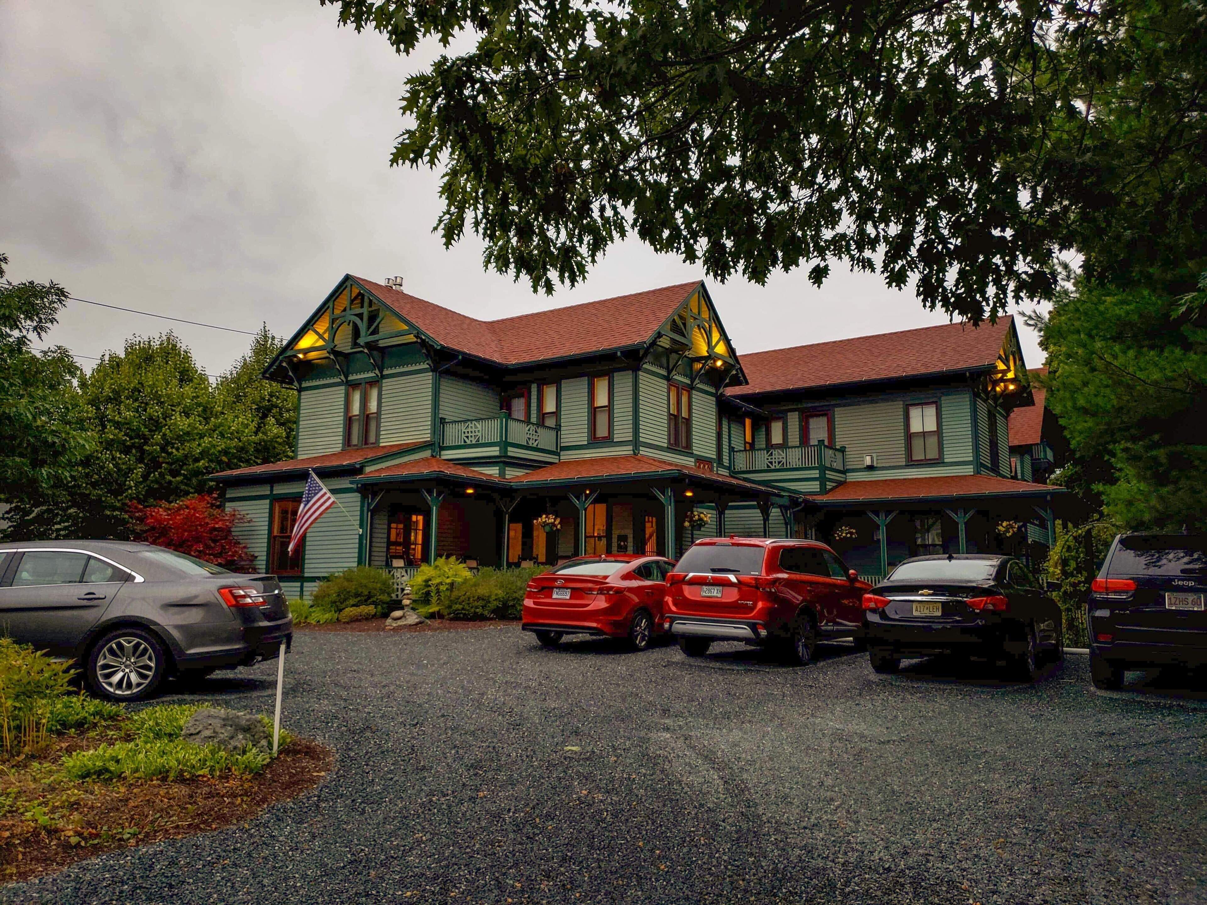 Um edifício de dois andares com fachada verde e telhado vermelho, apresentando um alpendre com vários carros estacionados na frente.