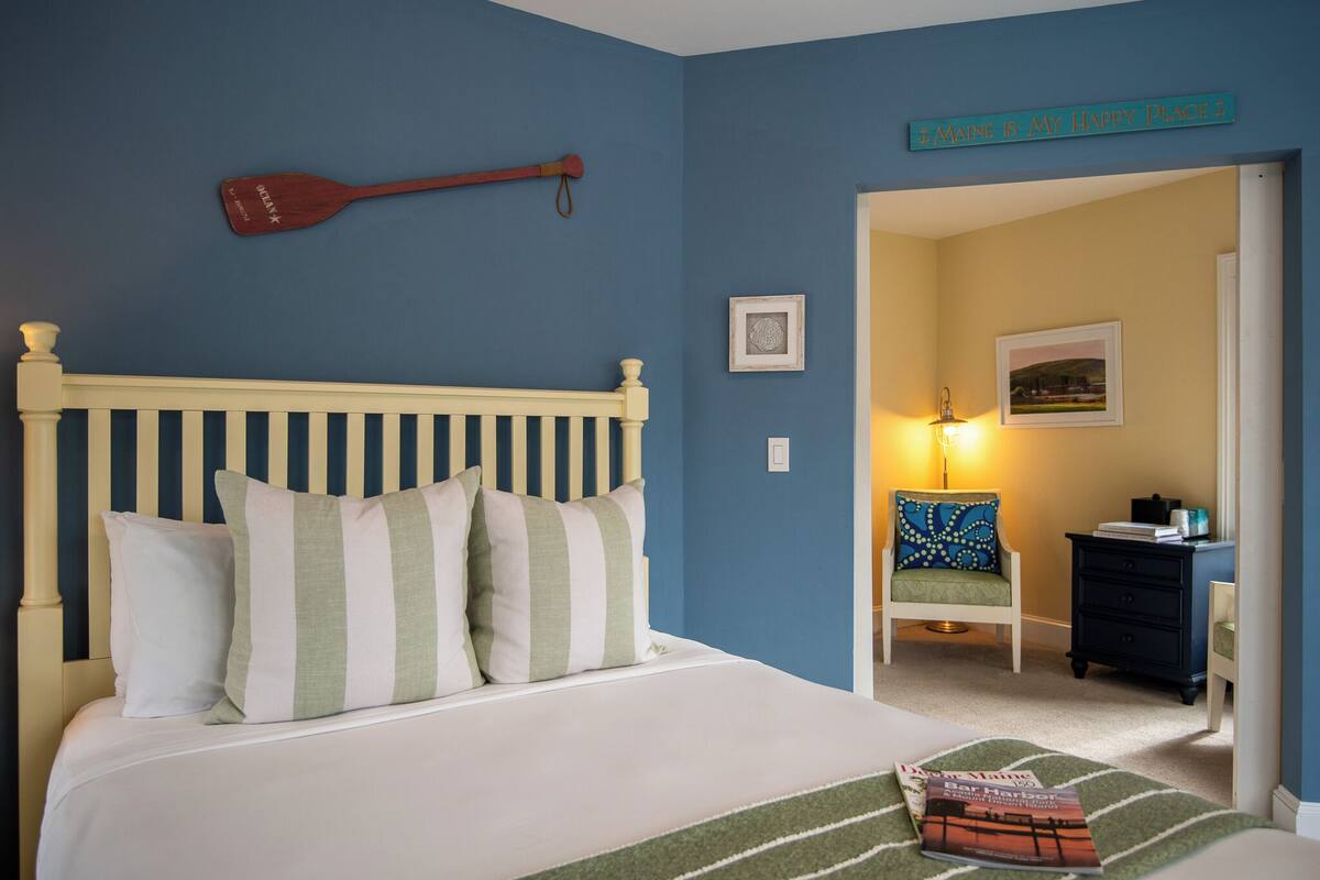Quarto com cama, almofadas, remo de madeira, cadeira, mesa de cabeceira e placa na parede.