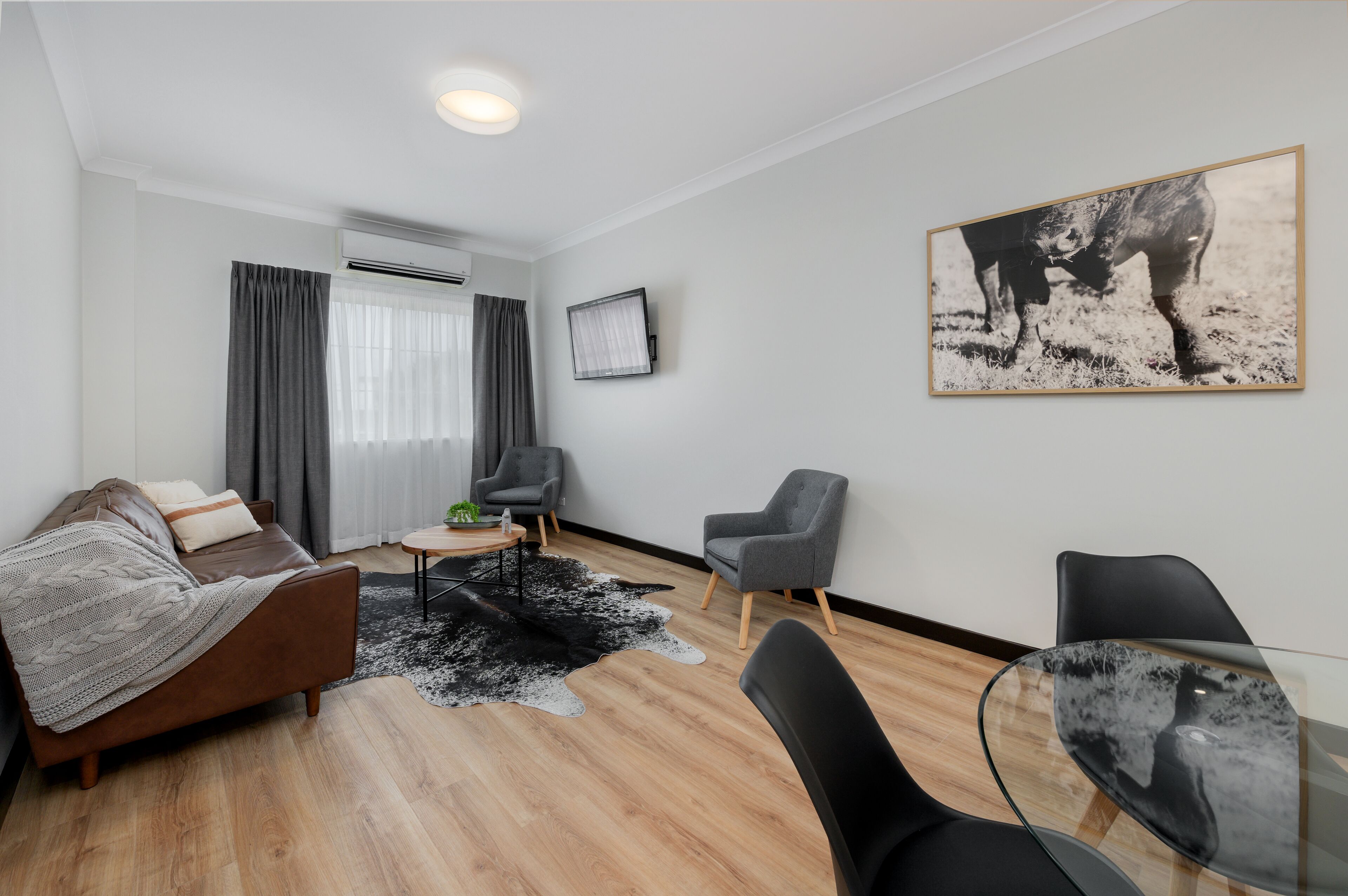 Uma sala de estar moderna com um sofá, cadeiras, uma mesa de centro de vidro e uma obra de arte em preto e branco na parede.