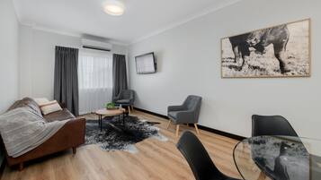Uma sala de estar moderna com um sofá, cadeiras, uma mesa de centro de vidro e uma obra de arte em preto e branco na parede.