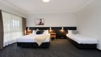 Quarto de hotel com duas camas, uma janela grande com cortinas, um quadro na parede e piso coberto por carpete.