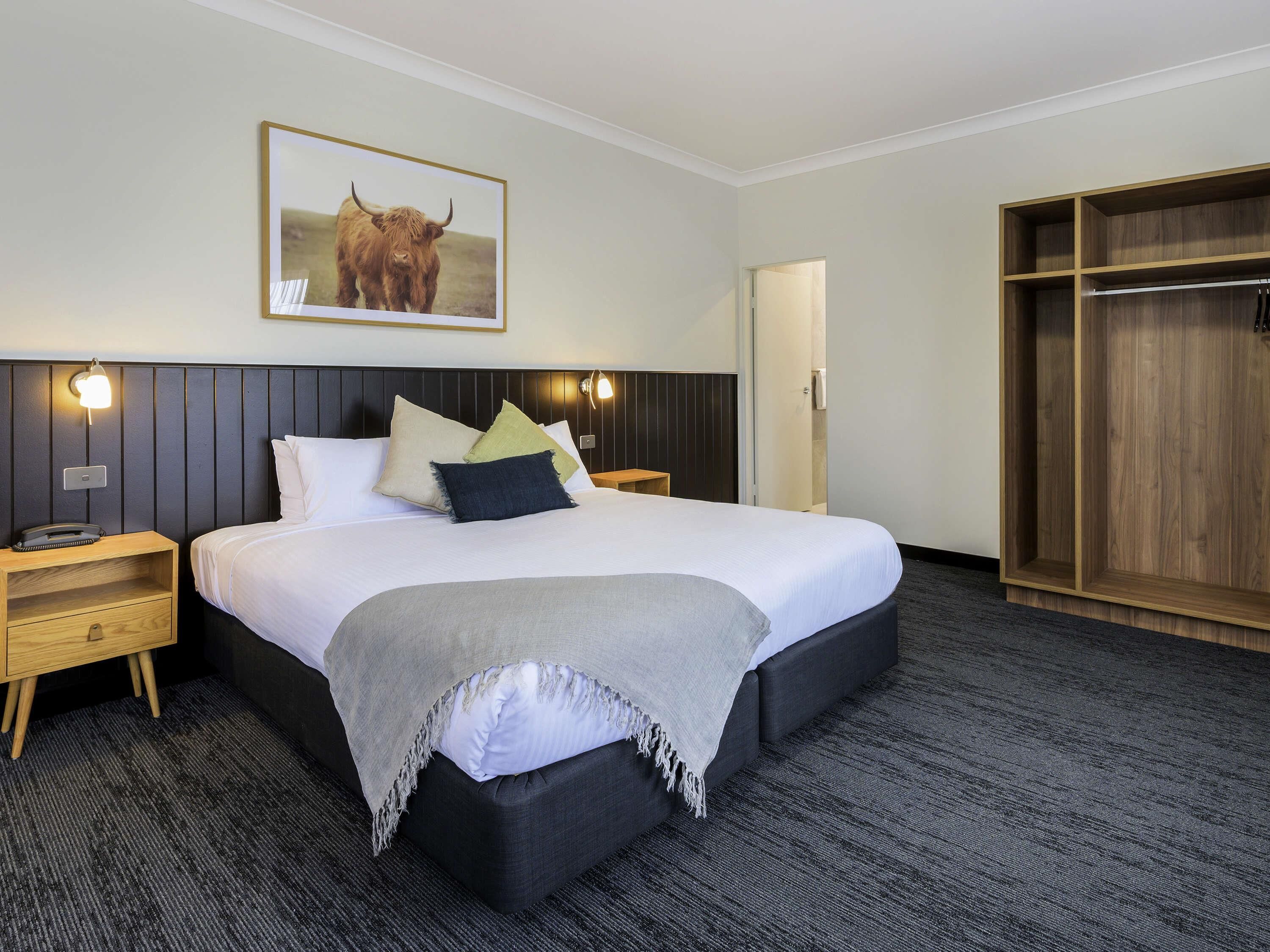 Quarto de hotel com cama, mesas de cabeceira, guarda-roupa e um quadro na parede.