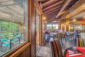 Um restaurante com vigas de madeira, janelas amplas e cadeiras coloridas.