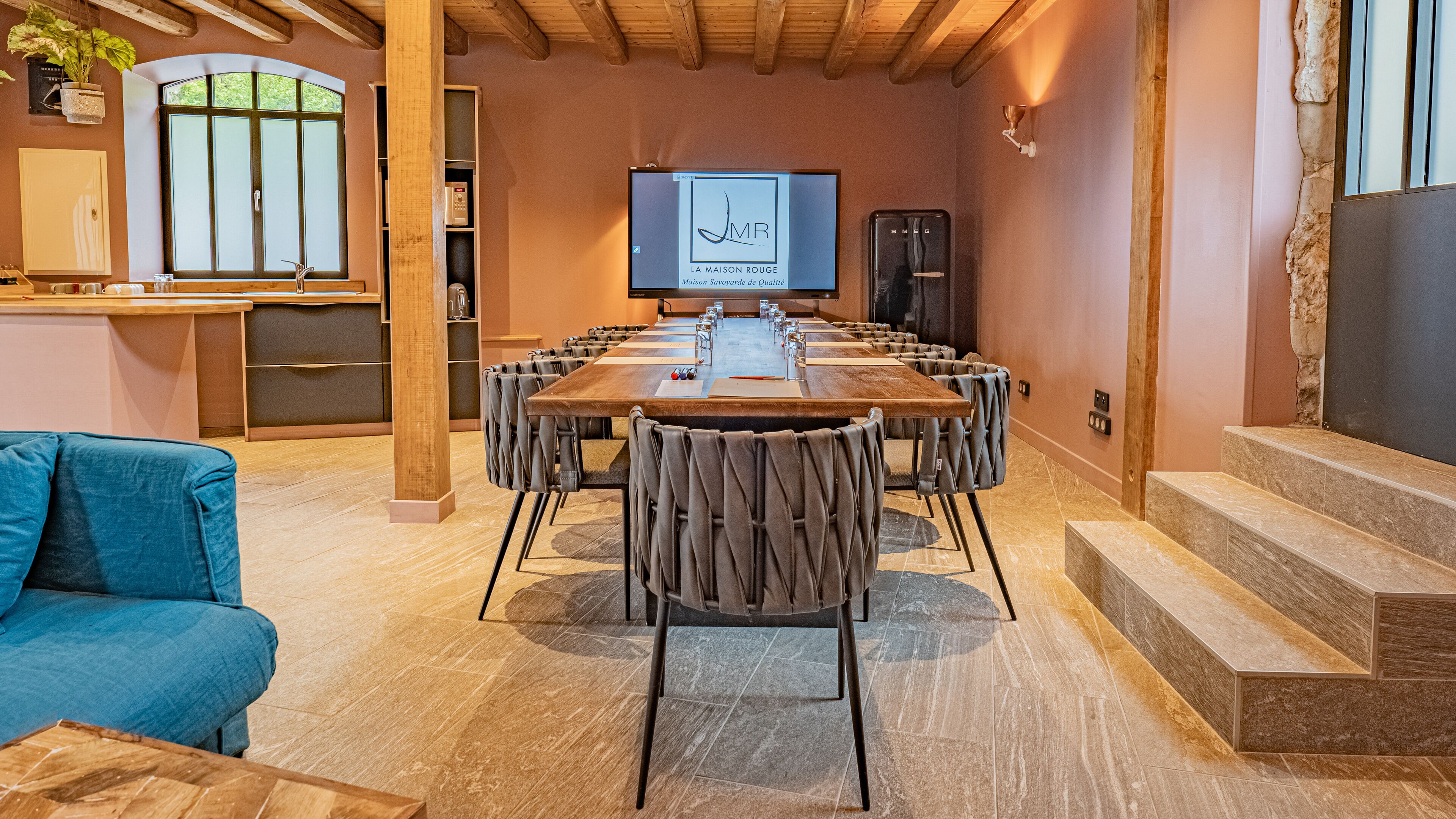 Uma sala de conferência com uma mesa comprida, cadeiras e uma tela exibindo um logotipo.