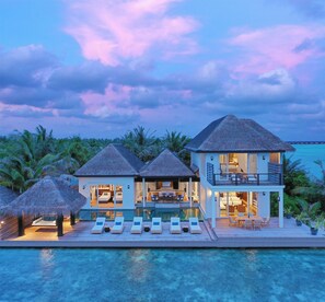 Um resort com bangalôs sobre a água, piscina e vista para o oceano.