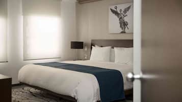 Quarto de hotel com uma cama grande, uma mesinha de cabeceira, uma luminária e uma obra de arte na parede.