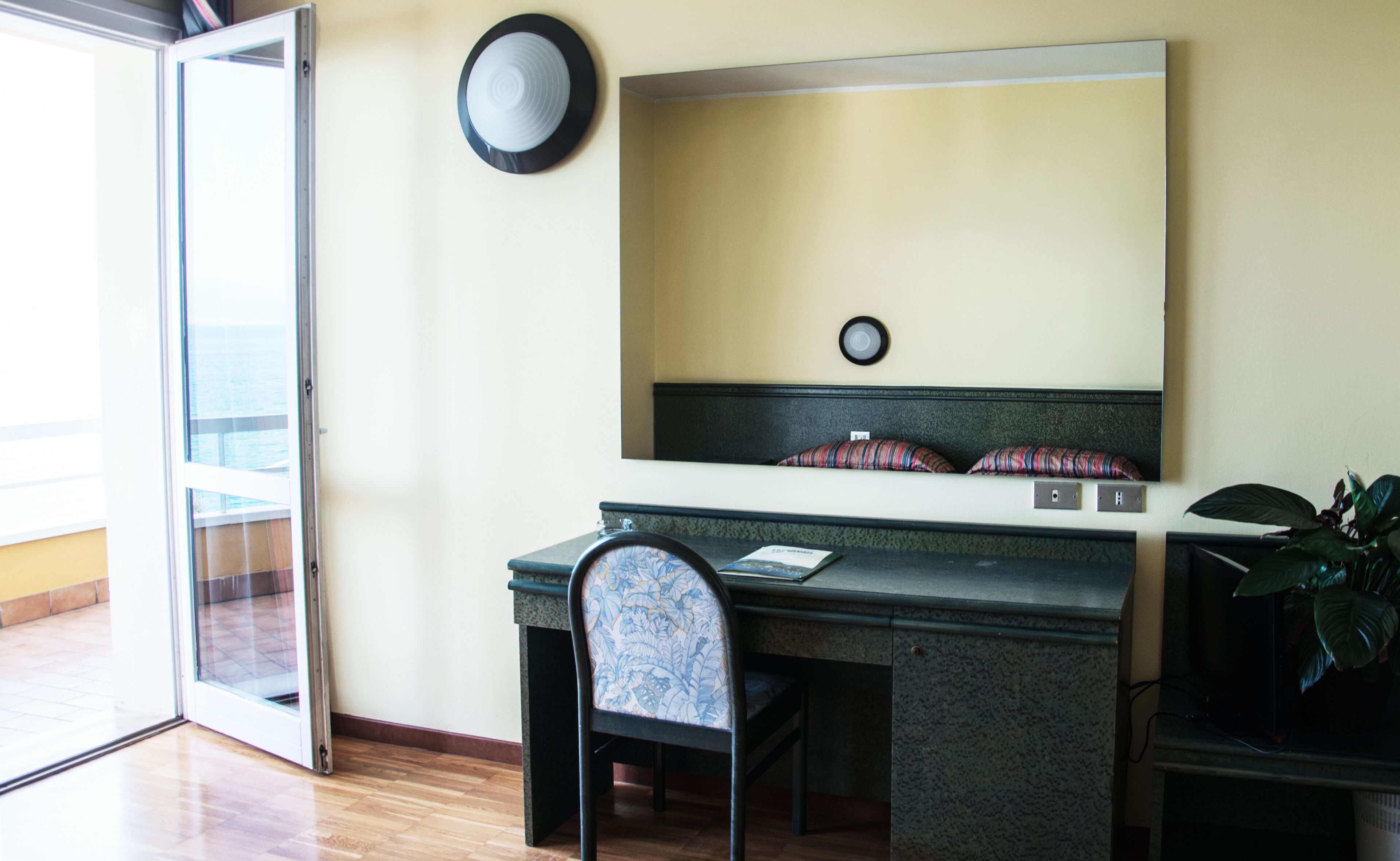 Quarto de hotel com escrivaninha, cadeira e um espelho grande na parede.