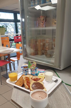 Uma bandeja de café da manhã com torradas, geleia, creme de chocolate, suco de laranja, leite e uma bebida com café.