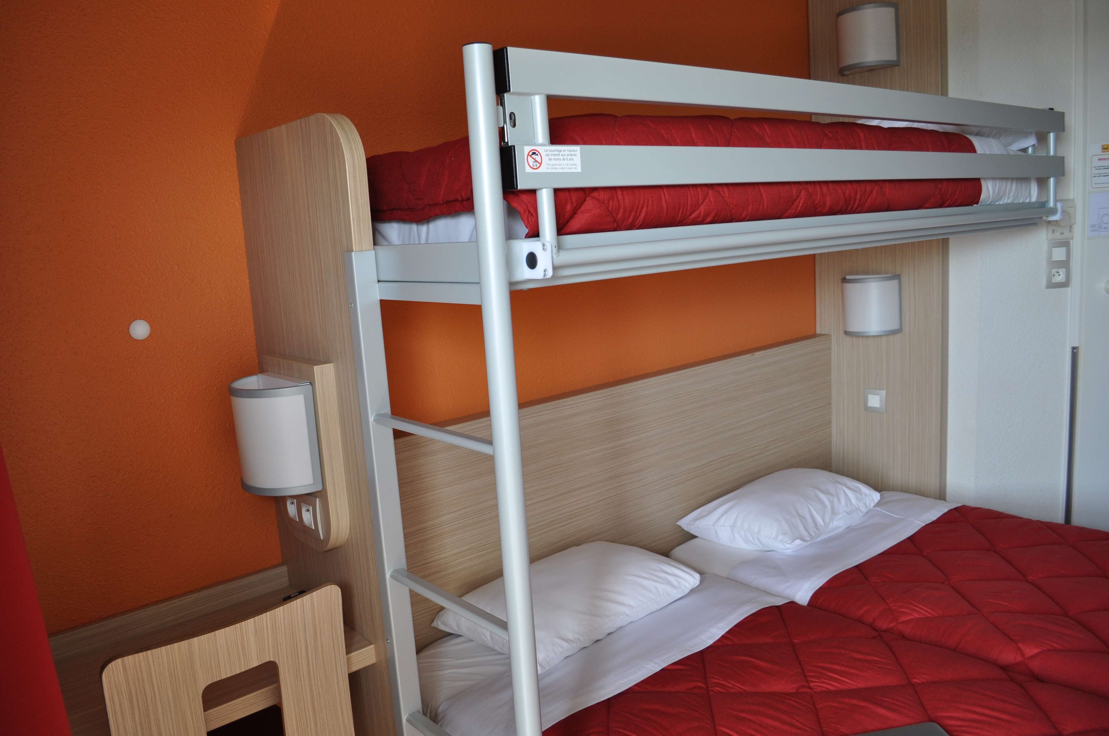Uma cama beliche com um cobertor vermelho, um travesseiro branco e um encosto de madeira.