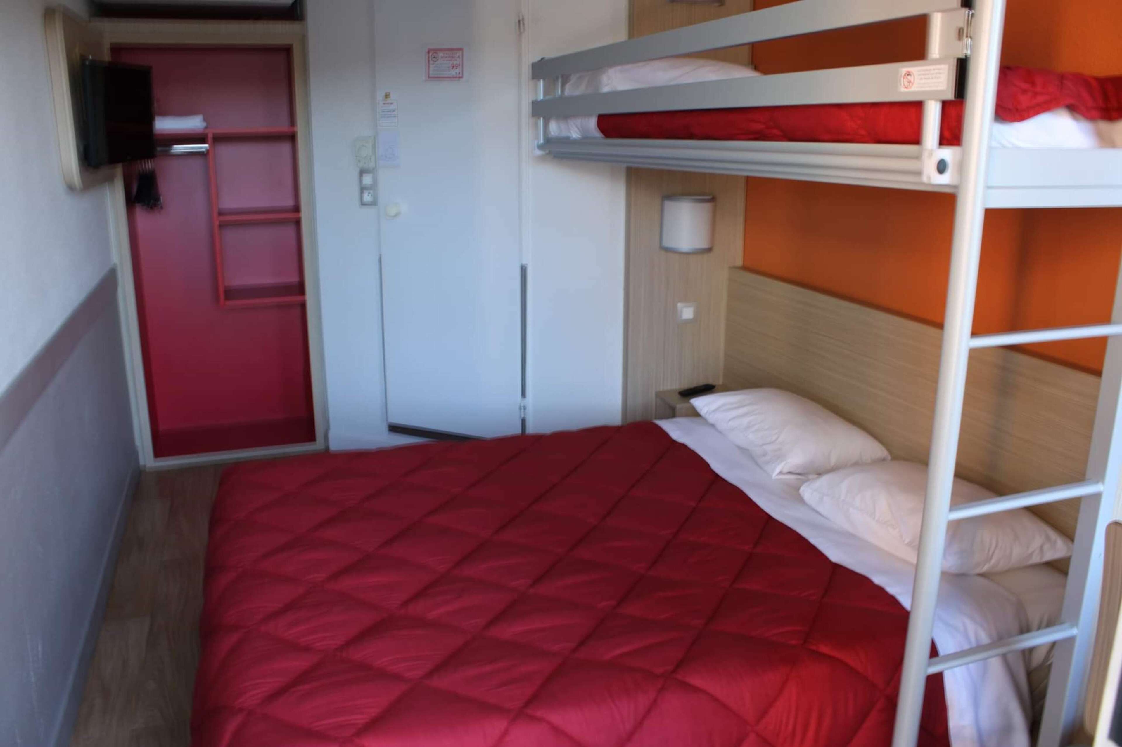 Uma cama de beliche com um edredom vermelho, uma porta vermelha e uma pequena mesa de cabeceira com abajur.