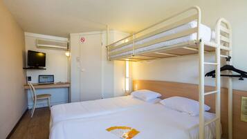 Quarto de hotel com beliche, escrivaninha e computador, além de televisão.