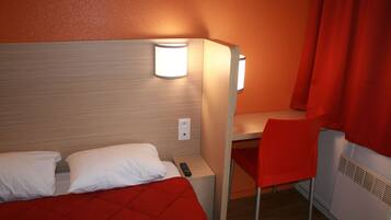 Quarto de hotel com cama, escrivaninha e uma cadeira. Há um controle remoto na escrivaninha.