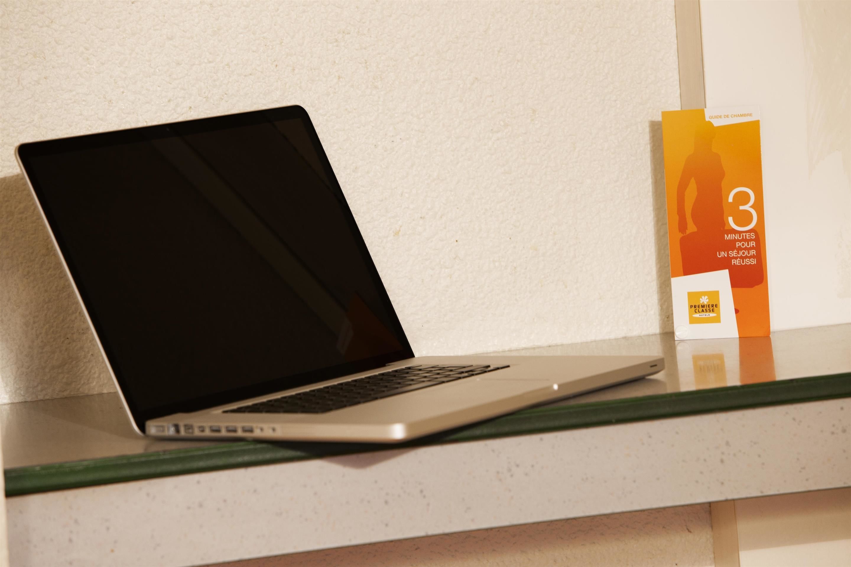 Um laptop numa prateleira de vidro com um livro intitulado "3 minutes pour un séjour réussi" ao lado.