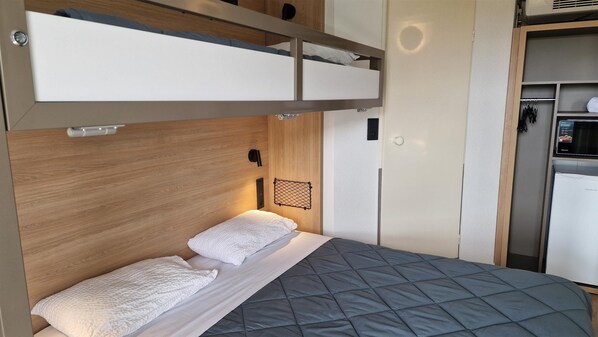 Uma cama beliche com cabeceira de madeira, uma prateleira pequena e uma luminária fixada na parede.