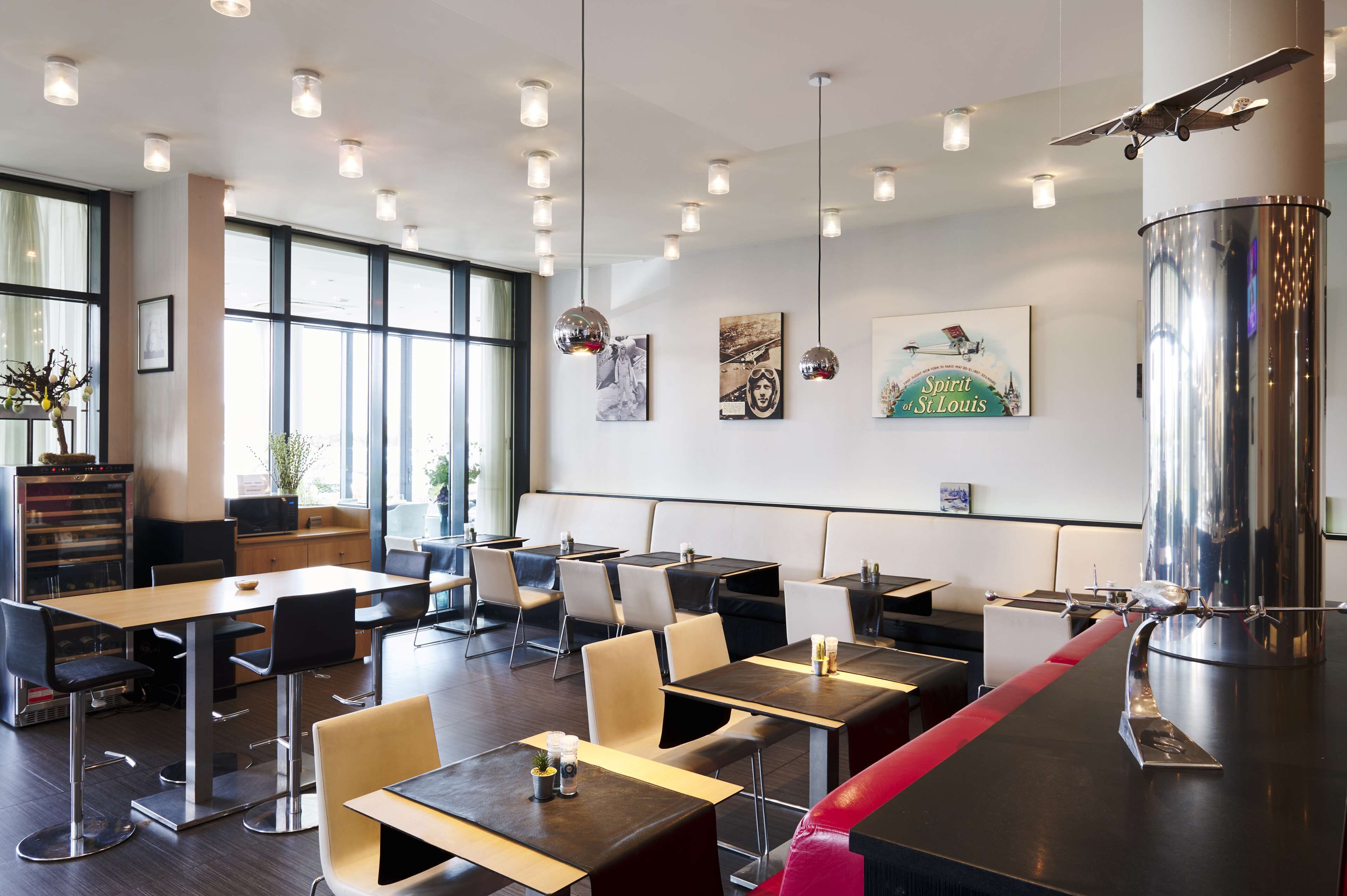 Um restaurante moderno com várias mesas e cadeiras, janelas amplas e obras de arte nas paredes.