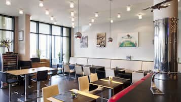 Um restaurante moderno com várias mesas e cadeiras, janelas amplas e obras de arte nas paredes.