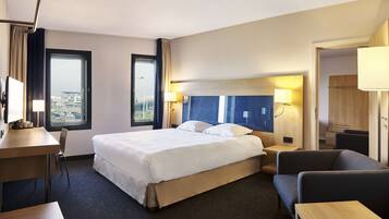 Quarto de hotel com uma cama grande, uma mesa, uma cadeira e vista para a cidade pela janela.
