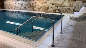 Piscina com parede de pedra ao fundo, escada metálica e uma cadeira de praia branca.