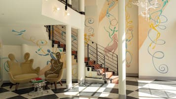 Um hall amplo com piso xadrez, uma escadaria com arte abstrata nas paredes e uma área de estar com design de assento exclusivo.