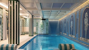 Uma área de piscina com piso ladrilhado, piscina e parede com figuras decorativas.