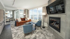 Quarto de hotel moderno com lareira, sofá, área de jantar e grandes janelas com vista.