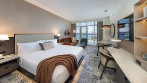 Quarto de hotel com uma cama grande, uma escrivaninha, uma cadeira e vista para o mar.