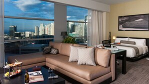 Quarto de hotel moderno com uma janela grande oferecendo vista da cidade, um sofá, uma cama e uma mesa de centro com comodidades.