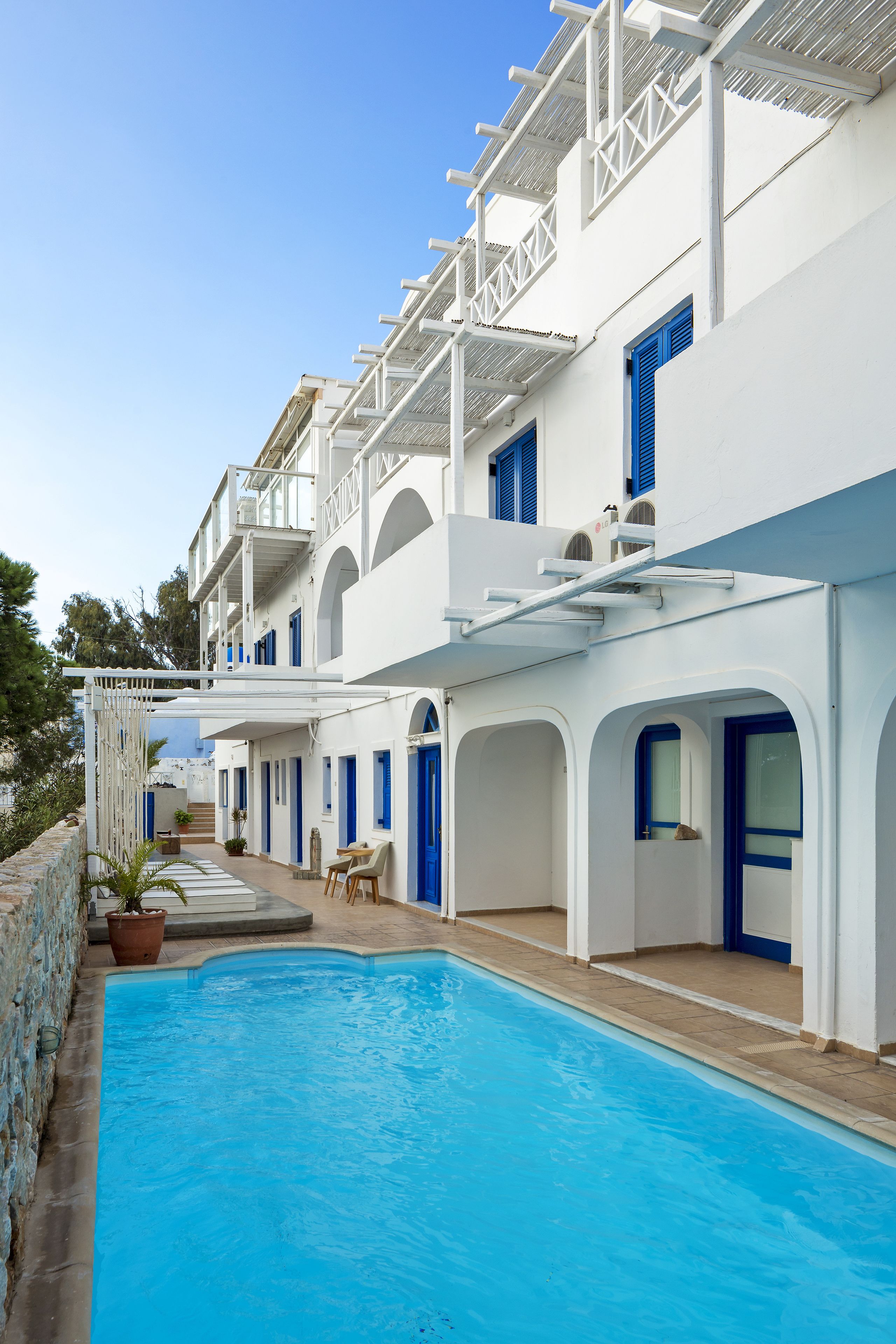 Um edifício branco com detalhes azuis, uma piscina e uma área coberta ao ar livre.
