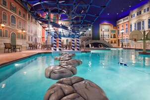 Piscina interna com uma formação rochosa no centro, cercada por uma área de lazer com cadeiras e um aro de basquete.