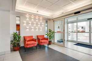 Uma área de recepção com duas cadeiras vermelhas, um luminário fixado na parede e uma porta de vidro que dá para o exterior.