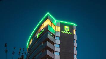 Edifício do Holiday Inn com design moderno, com vários andares e um grande letreiro de neon verde.