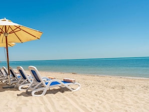 Uma praia com espreguiçadeiras e um guarda-sol amarelo.