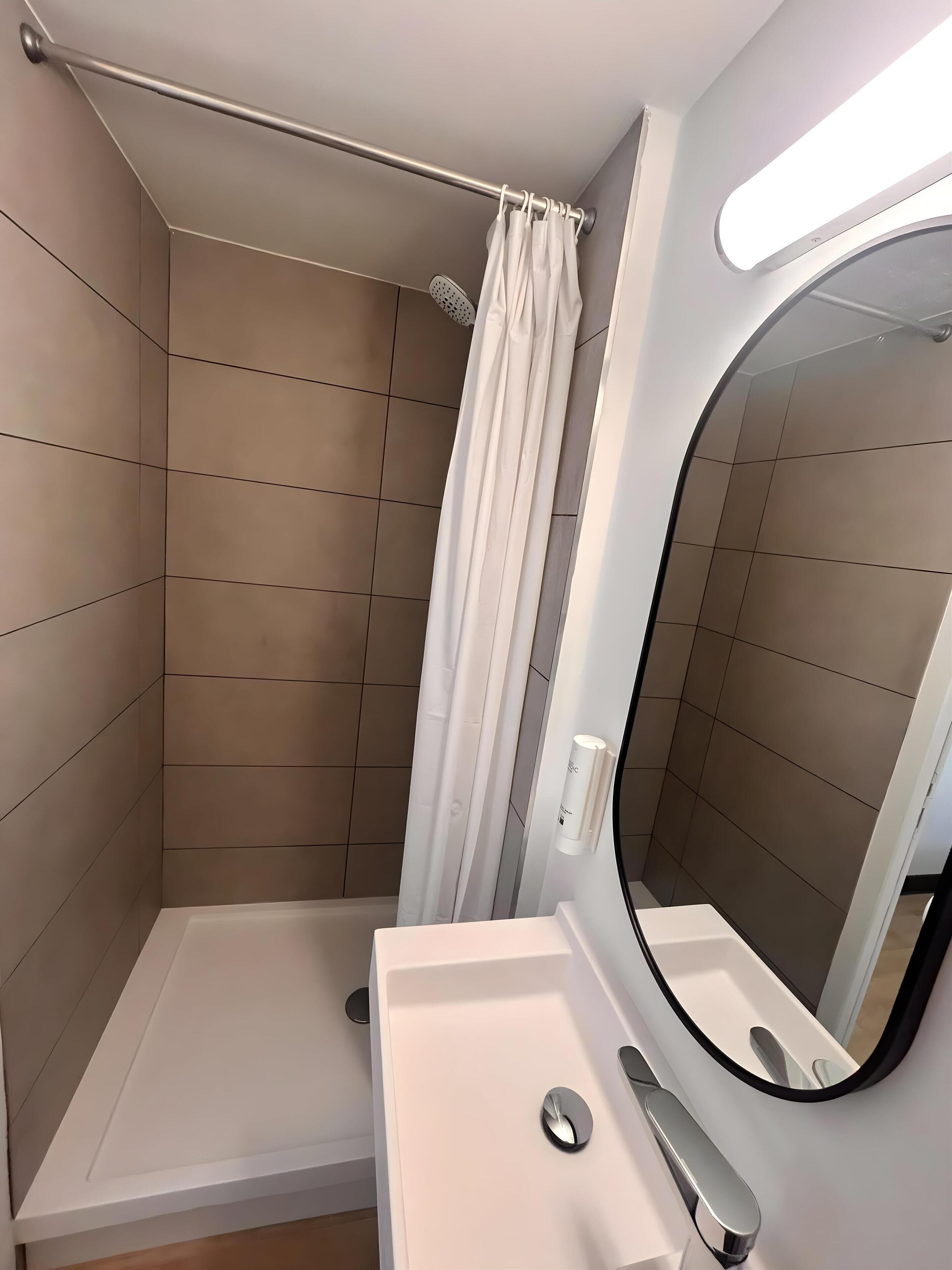 Uma casa de banho moderna com chuveiro, pia com espelho e porta-toalhas.