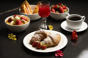 Uma mesa escura com croissants, morangos, um copo de suco vermelho e uma xícara de café.