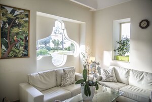 Uma sala de estar com um sofá branco, uma mesa de centro de vidro e uma pintura de uma árvore.