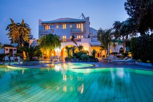 Um hotel com piscina, espreguiçadeiras e uma entrada bem iluminada.