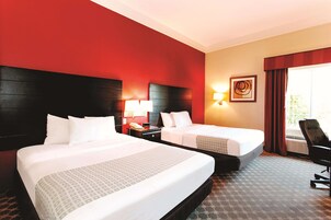 Quarto de hotel com duas camas, uma escrivaninha, uma cadeira e uma janela com cortinas.